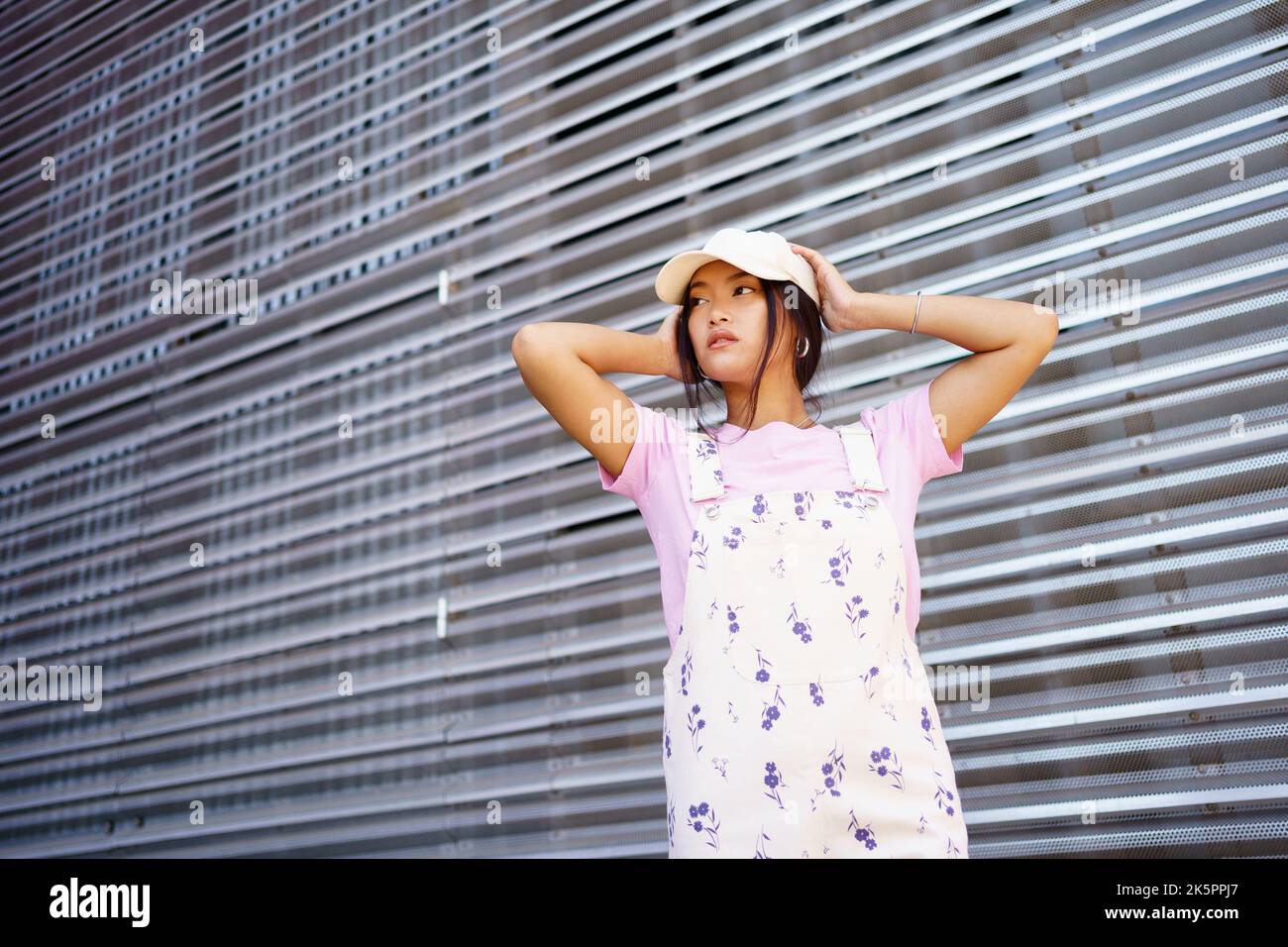 Low angle of glad Asian female in casual clothes, wearing cap, standing ...
