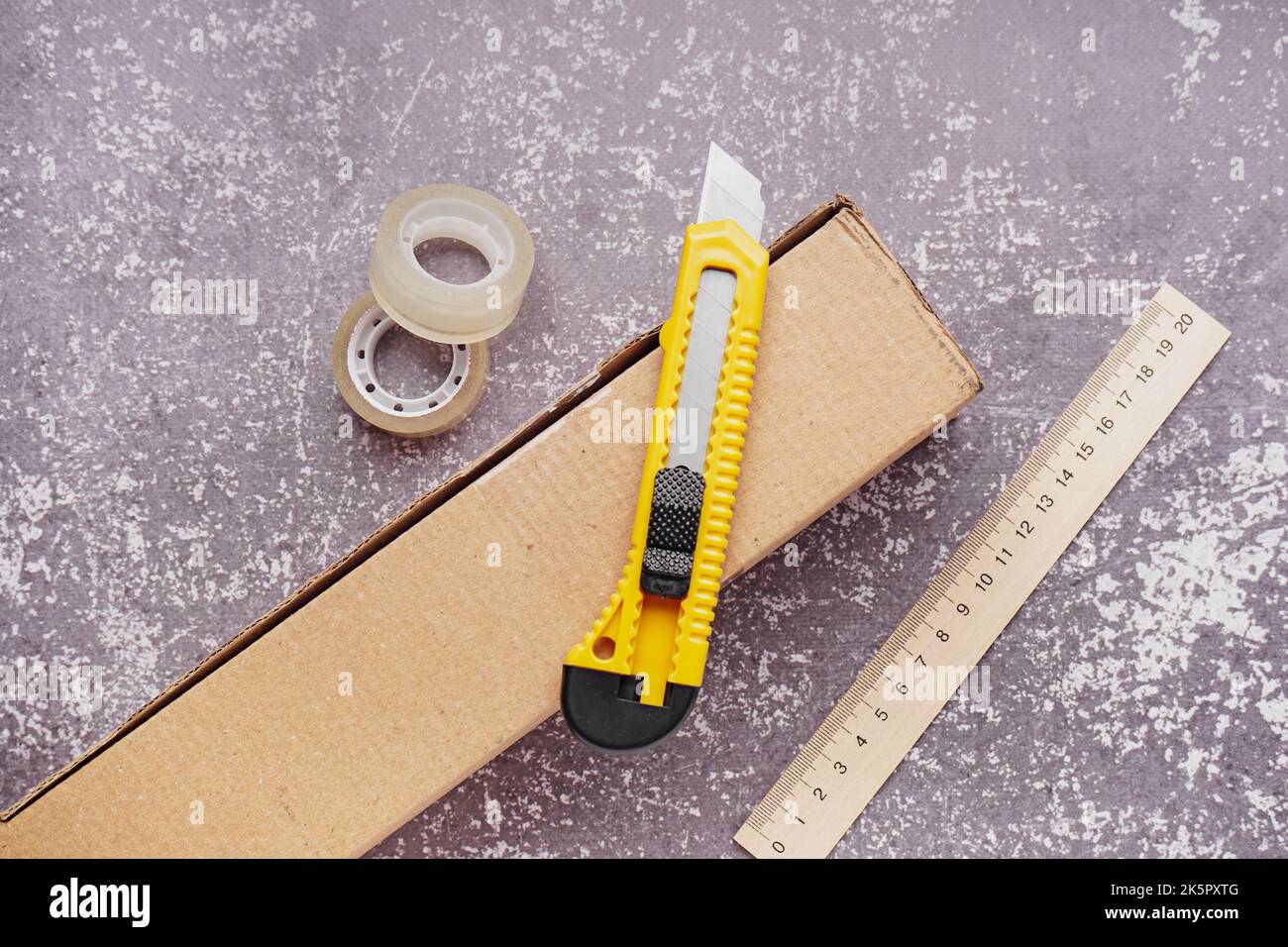 Utility knife with box, ruler and adhesive tapes on grunge background ...