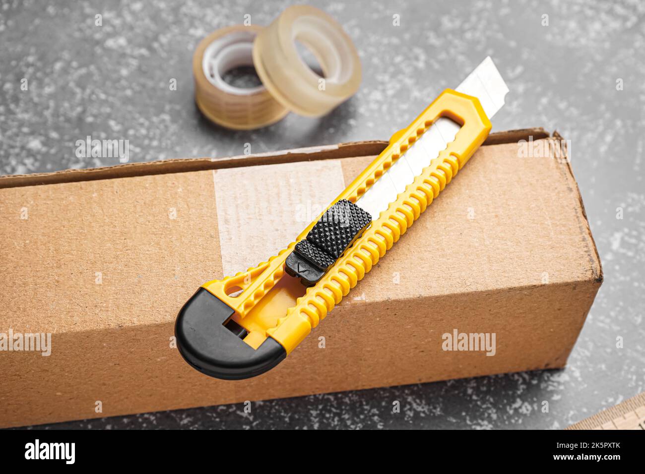 Utility knife with box, ruler and adhesive tapes on grunge background ...