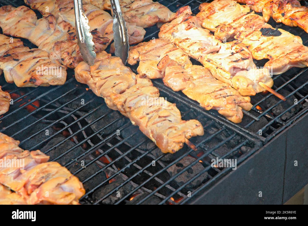 Grilling links and chicken and onions and potato cakes on open pit ...