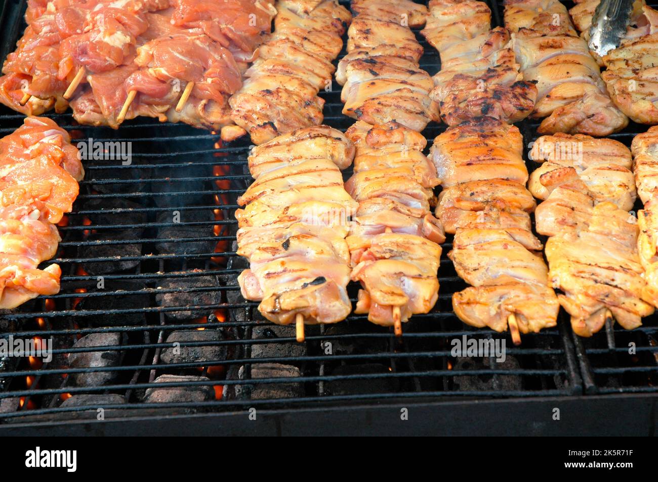 Grilling links and chicken and onions and potato cakes on open pit ...