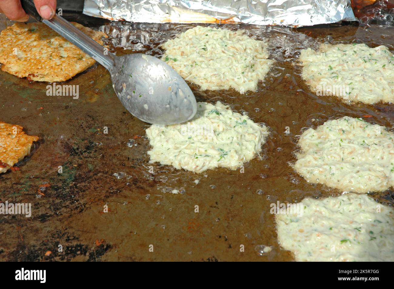 Grilling links and chicken and onions and potato cakes on open pit ...
