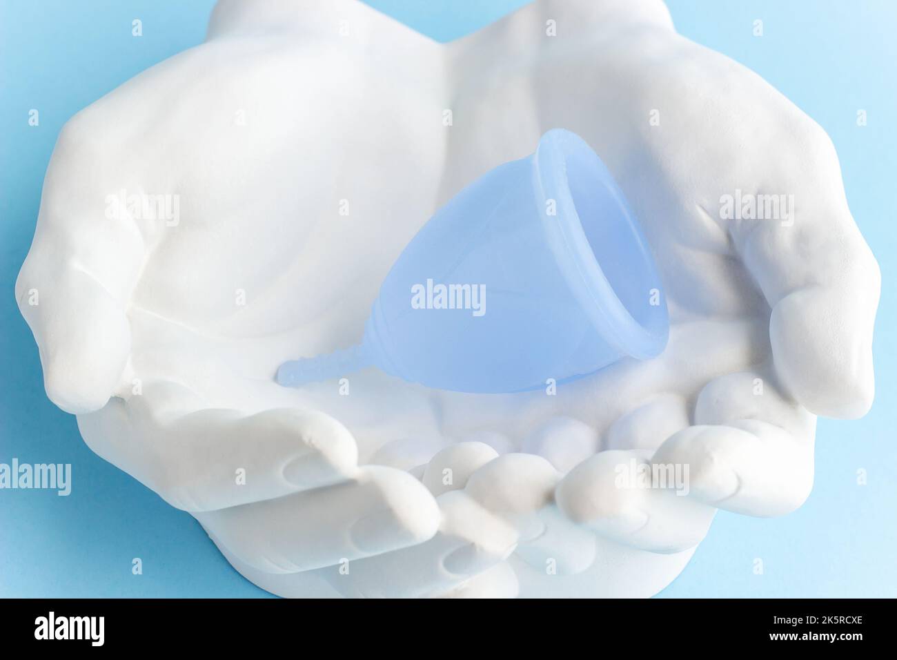 Blue menstrual cup in decorative plaster hands on blue background ...