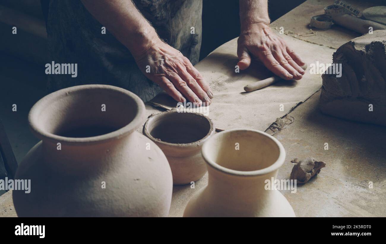Dirty hands of senior male ceramist are rolling small piece of clay on ...