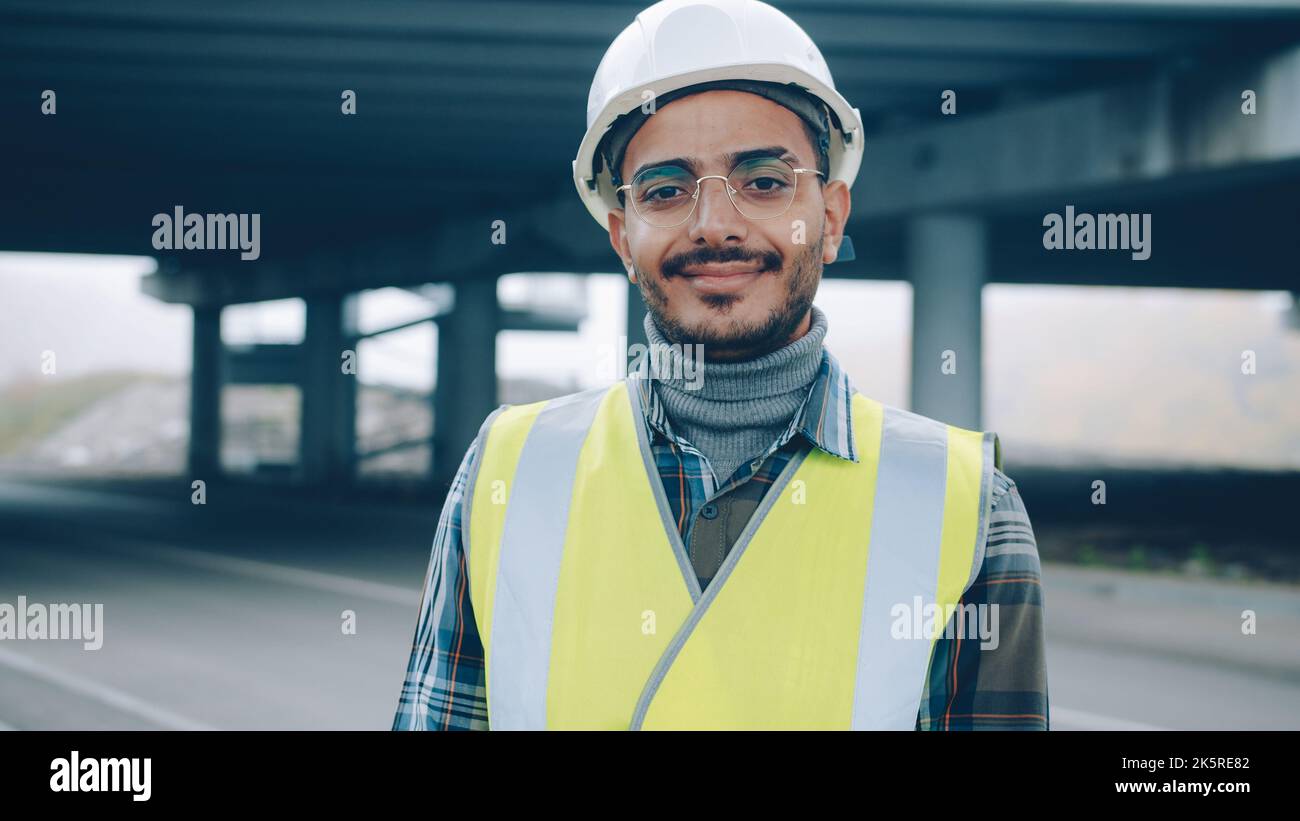 Joyful Arab guy wearing construction uniform is standing in urban ...