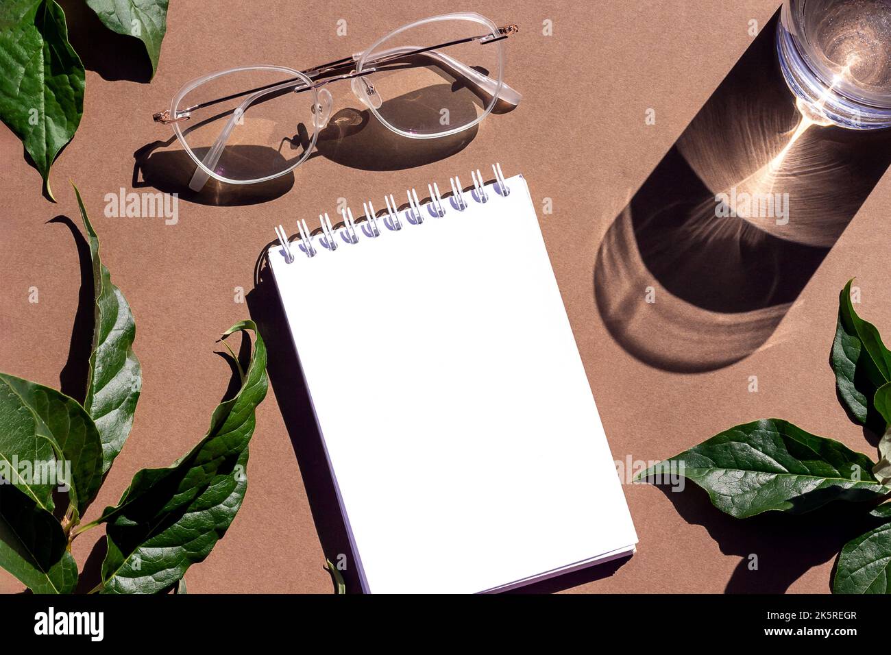 Empty notepad, glass of water and eyeglasses with strong shadows on ...