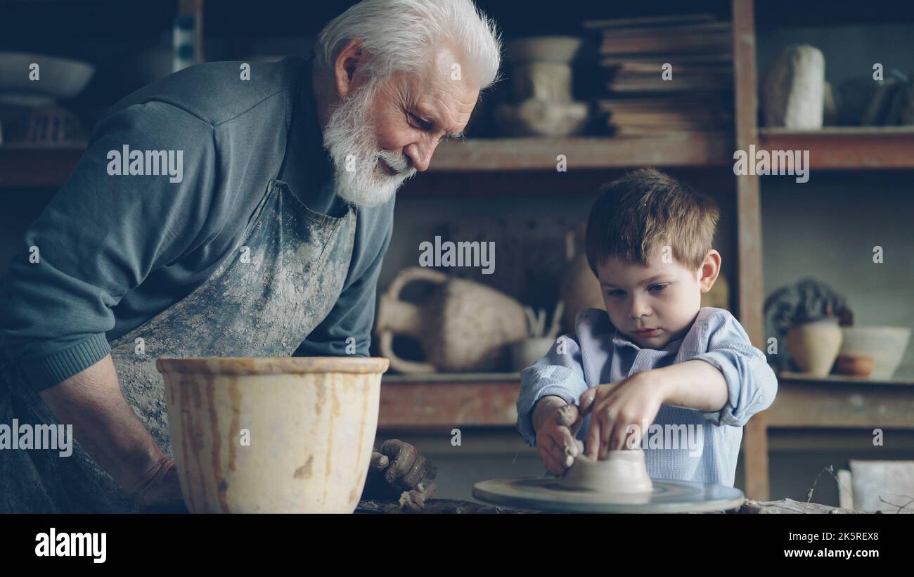 Concentrated young boy is molding clay into ceramic pot on spinning ...