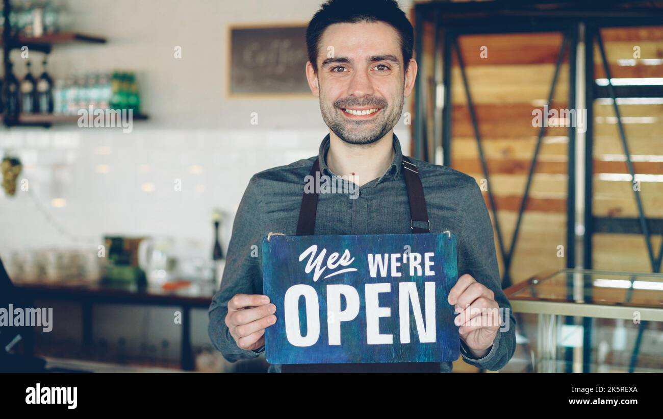 Cheerful handsome man small coffee-house owner is holding we are open ...