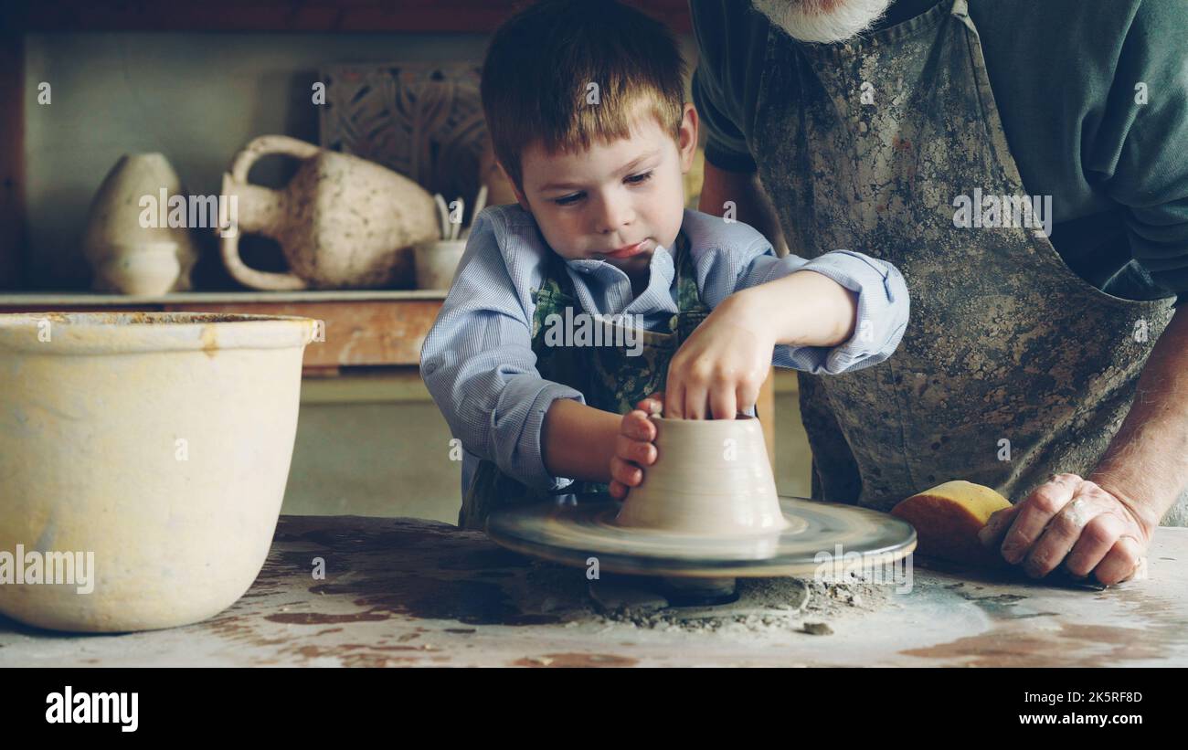 Curious little boy is learning pottery from his experienced grandfather ...