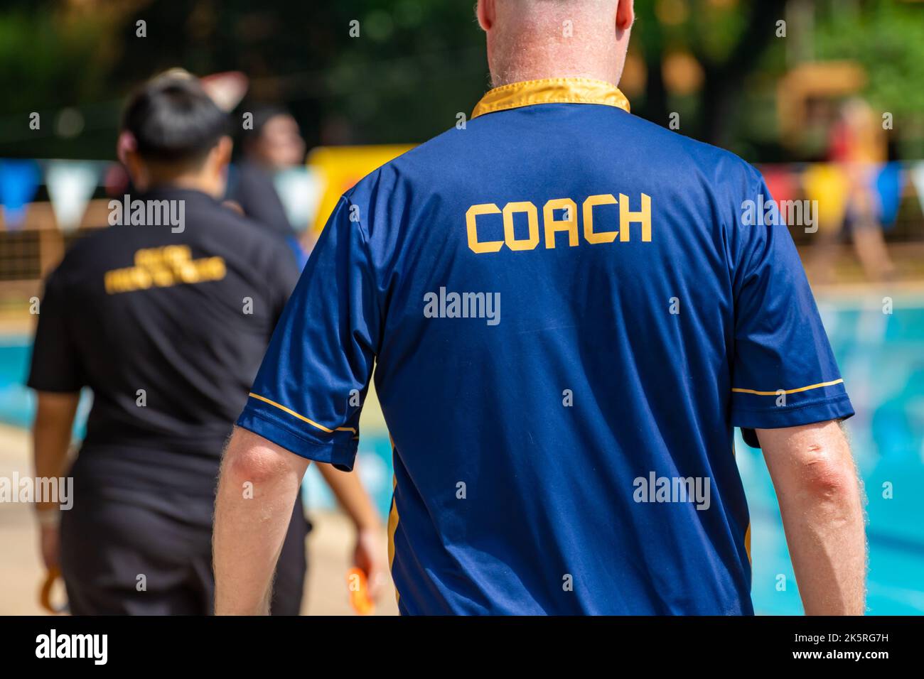 Back View Of Swimming Coaches Wearing Coach Shirt Working At An