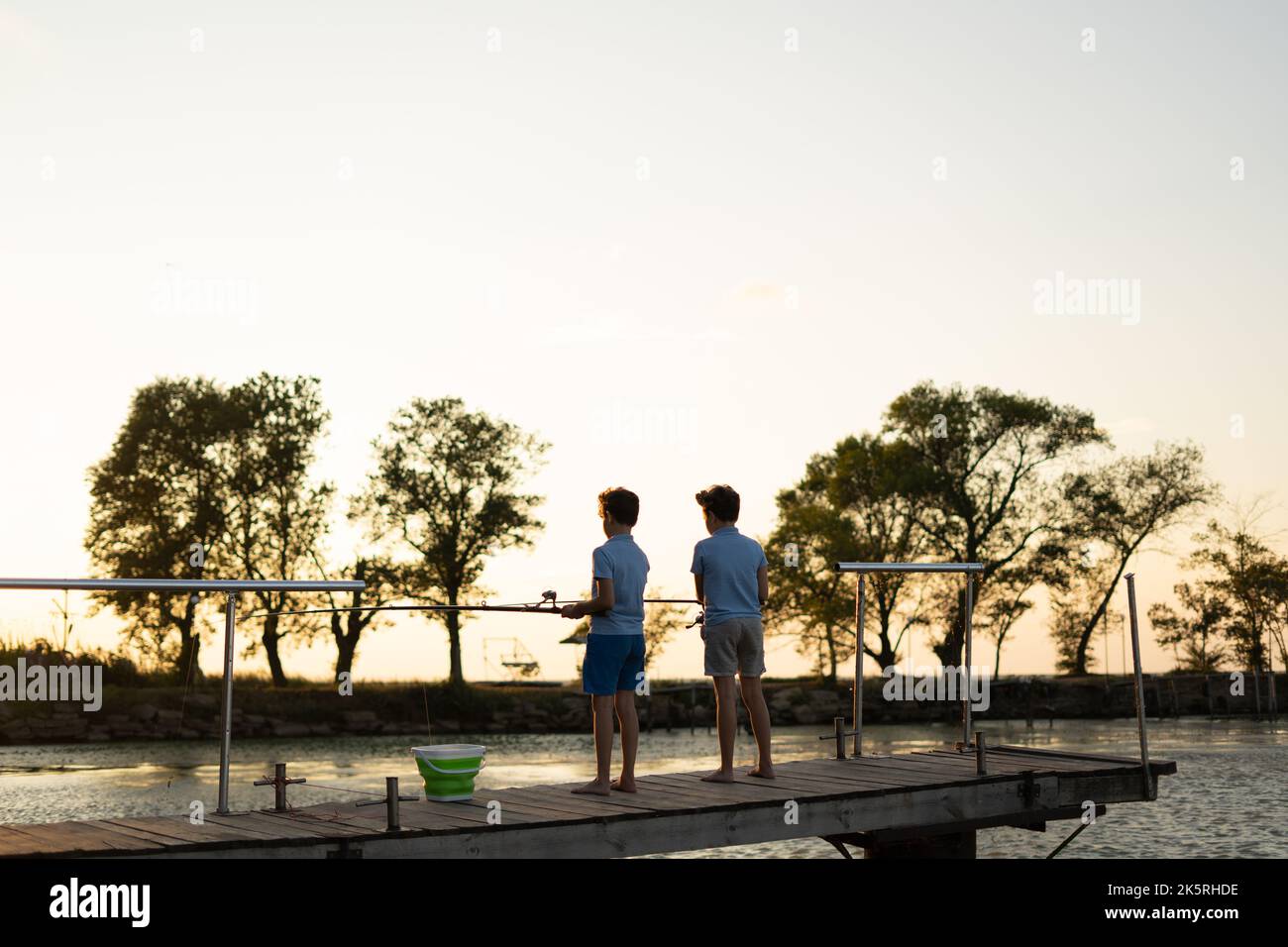 children with fishing rods stand on a wooden pier and fish at the lake. Fishing Stock Photo - Alamy