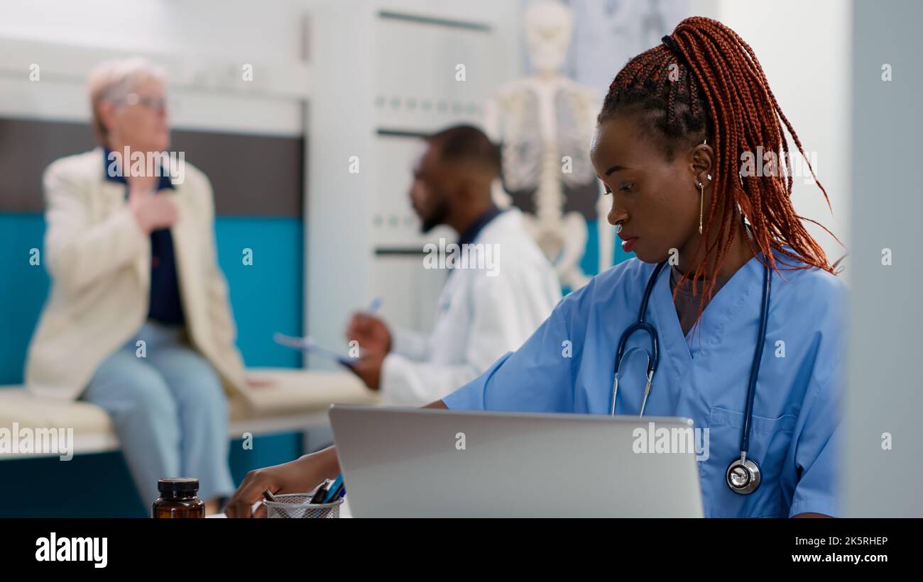 African american nurse working on appointments in cabinet, using laptop ...