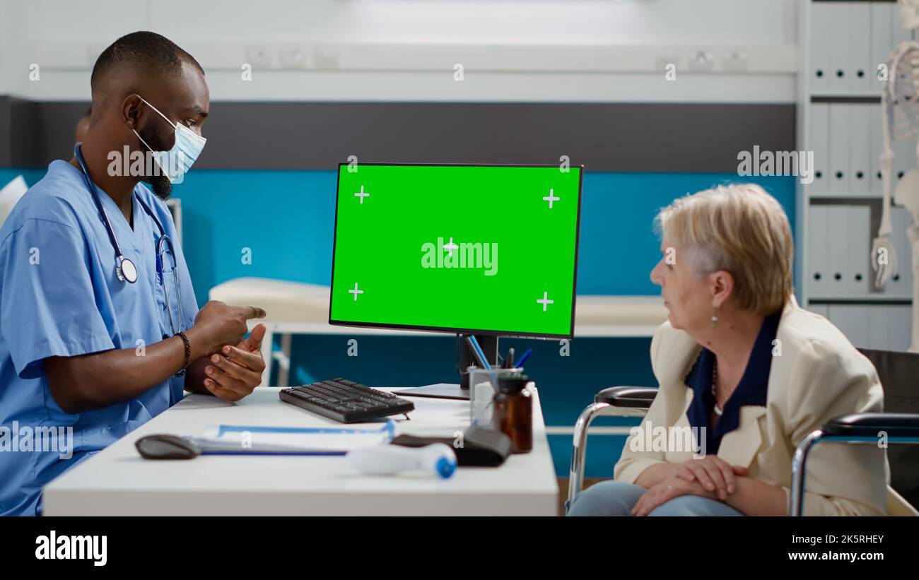 Assistant with face mask and woman in wheelchair using greenscreen ...