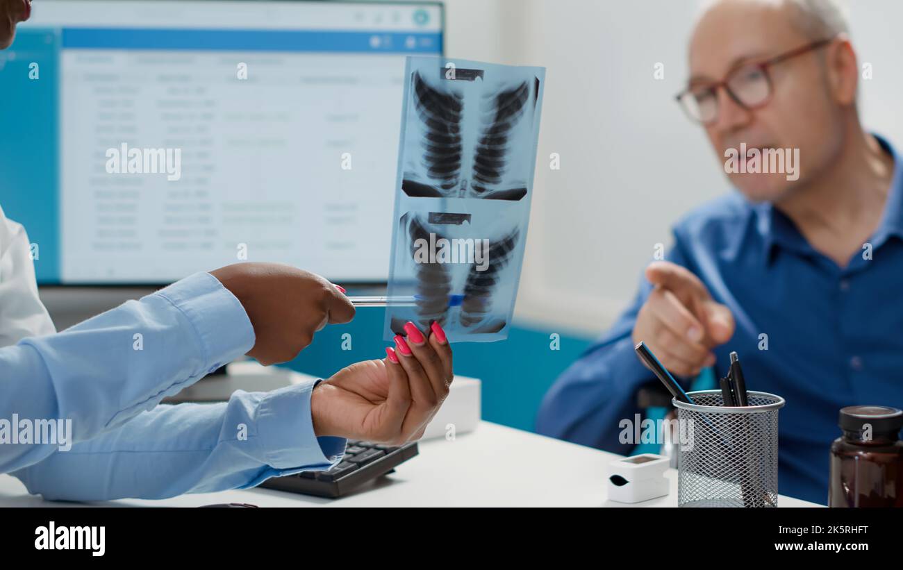 General practitioner analyzing x ray scan with senior man at checkup ...