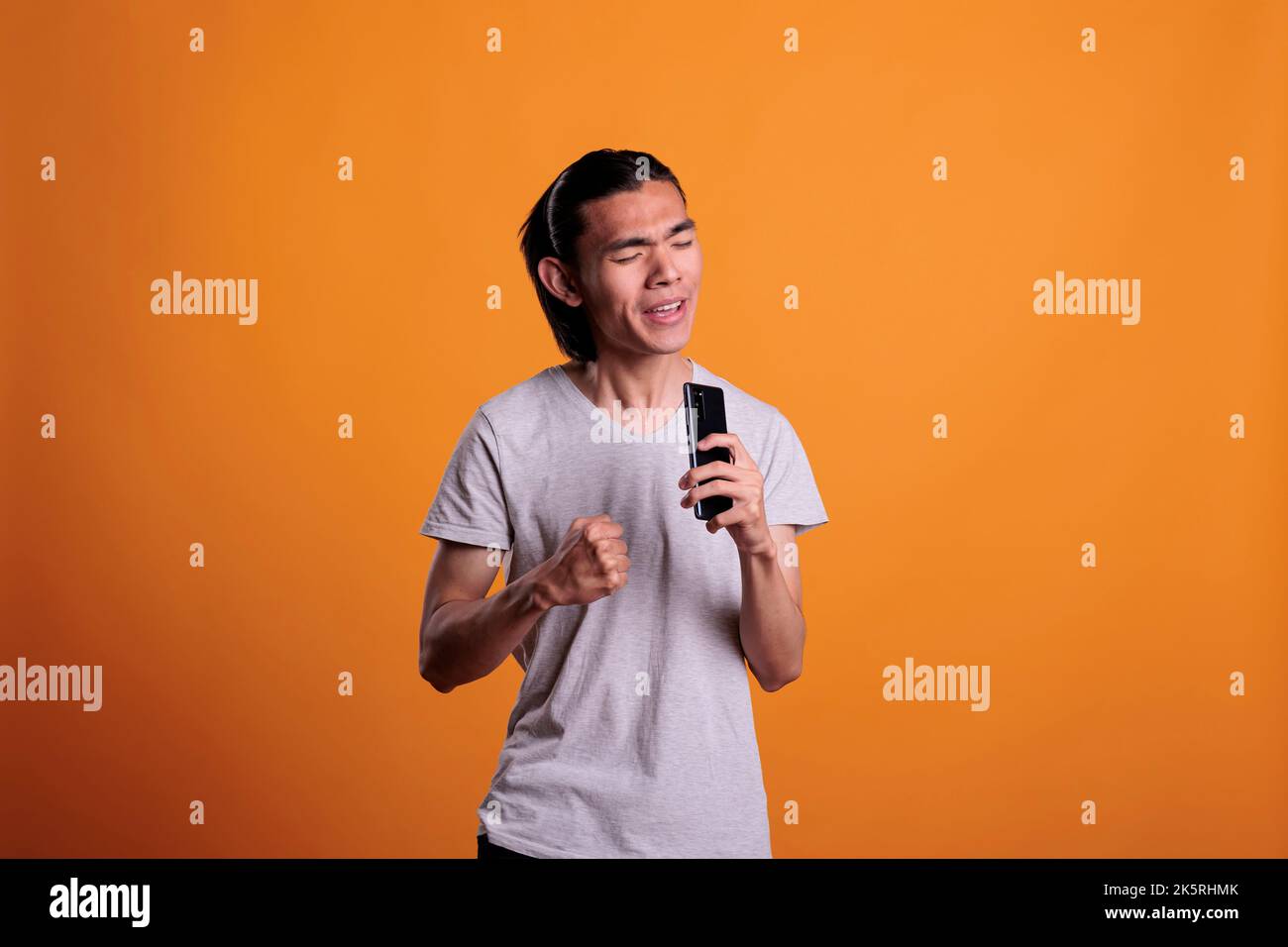 Young asian man singing karaoke, using smartphone as microphone. Singer ...