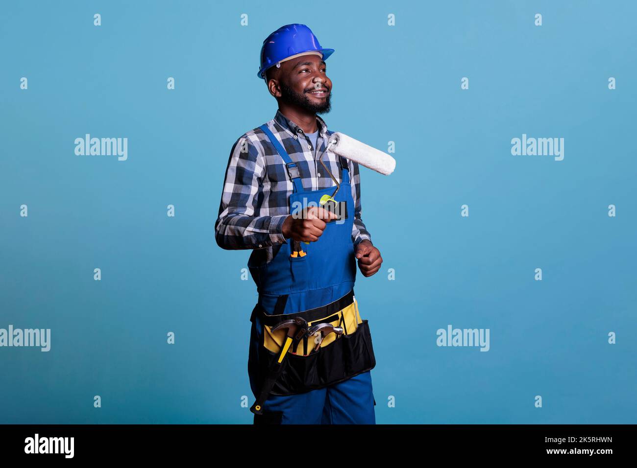 Happy construction worker holding paint roller performing interior ...