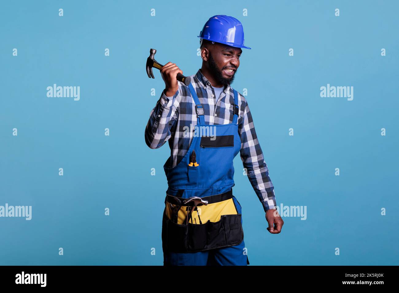 Aggressive builder holding hammer hard wearing blue protective helmet ...