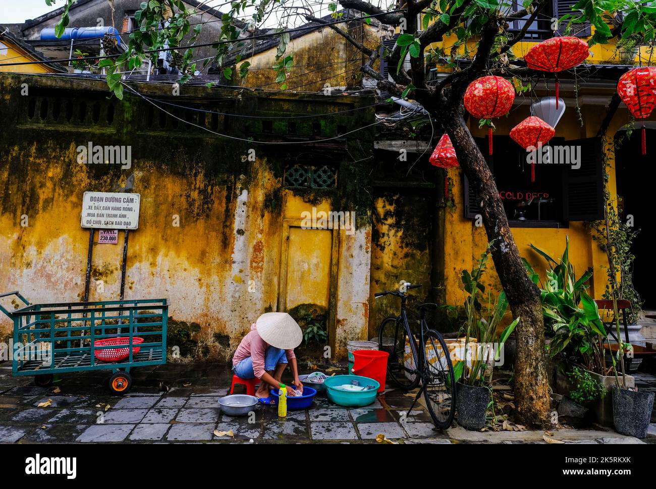 A Vietnamese woman washes up dishes iin front of an old building in the ...