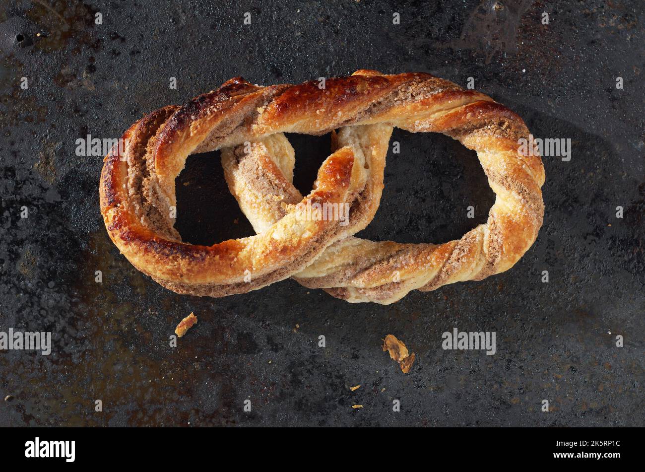 Single fresh pretzel with sugar on grunge iron background close-up, top ...
