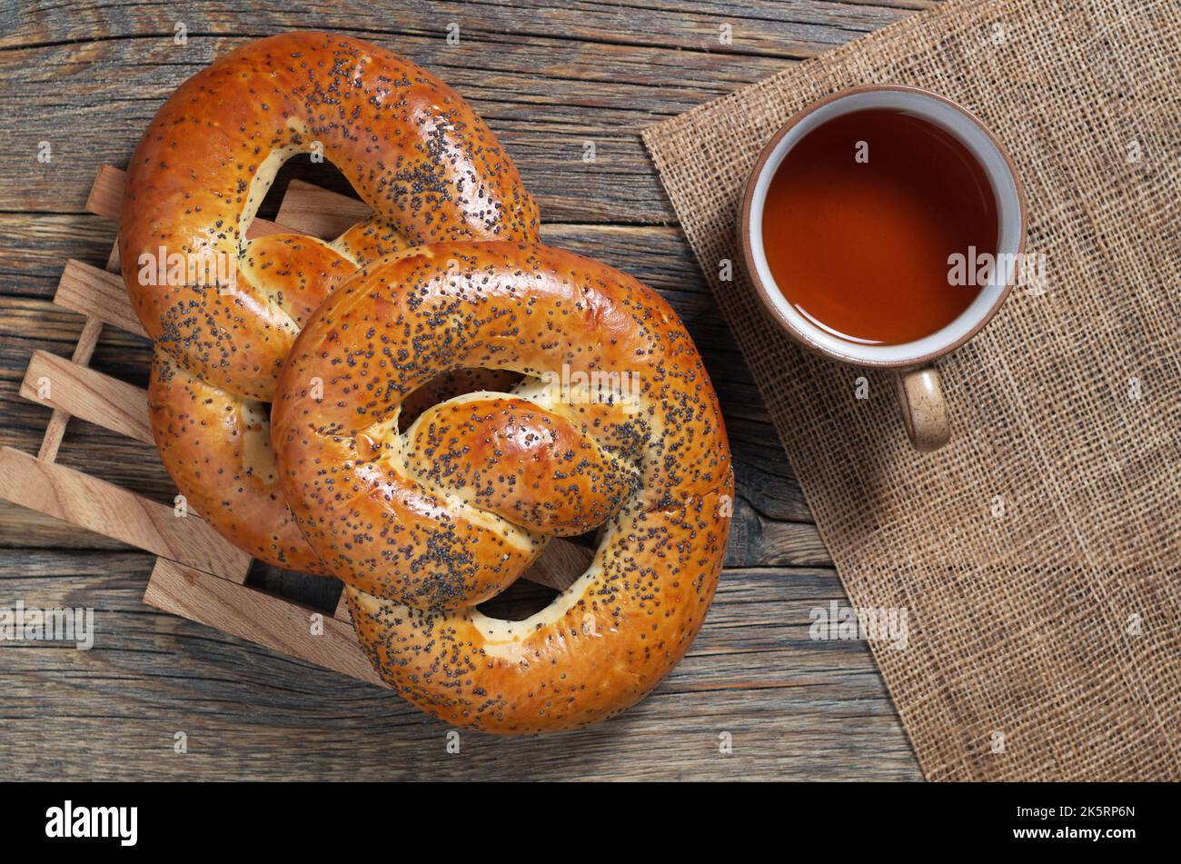 Soft pretzels with poppy and cup of tea on old wooden table, top view ...