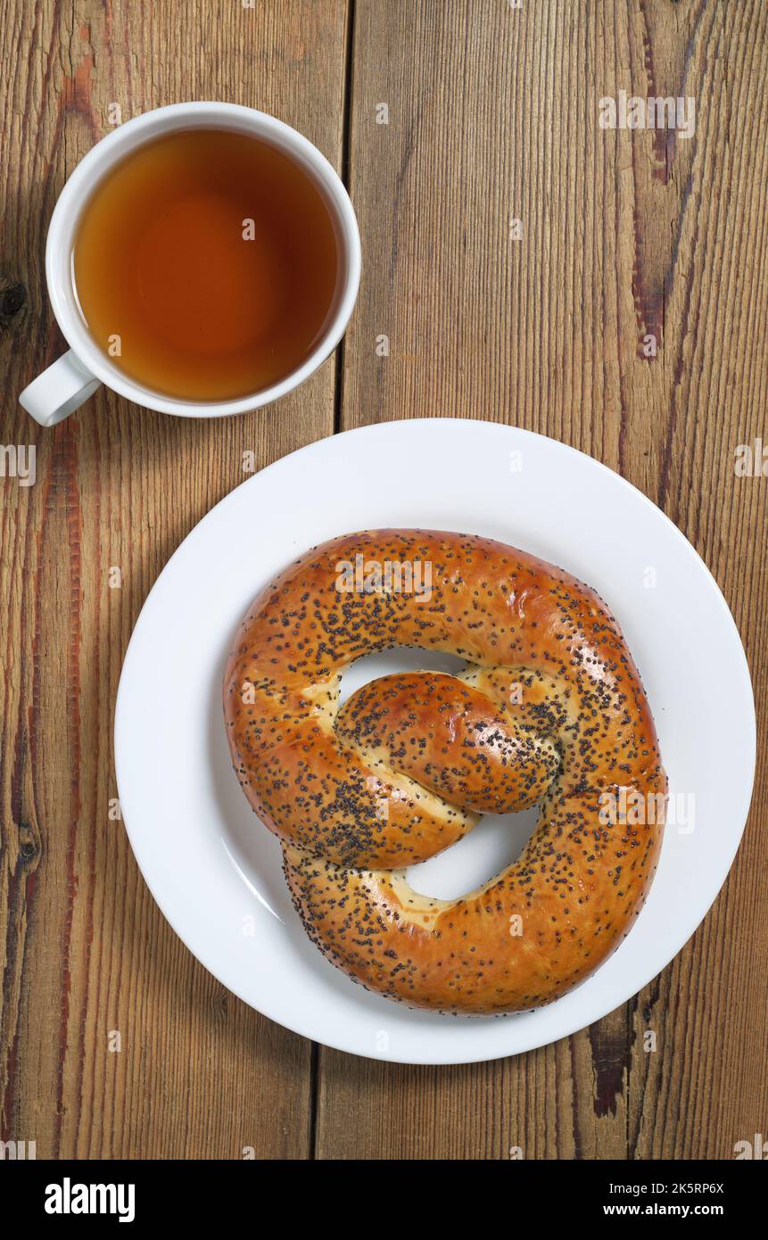 Soft poppy pretzels on white plate and cup of tea on wooden table, top ...