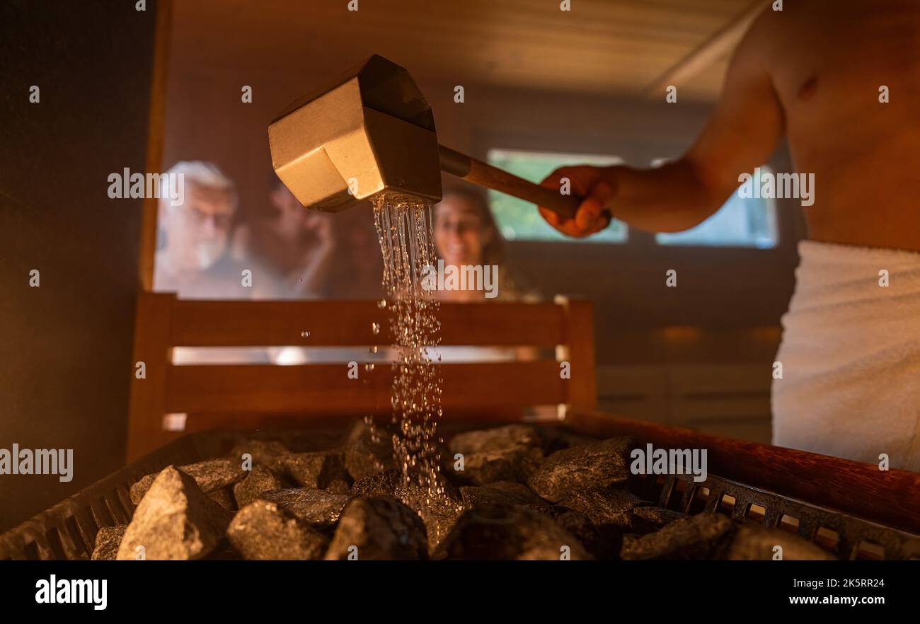 man pouring water onto hot stones with rain spoon in sauna room with a ...