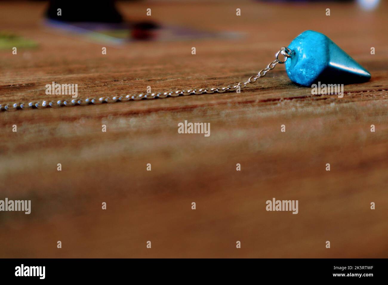 A close up shot of a blue crystal pendulum on a wooden surface with ...