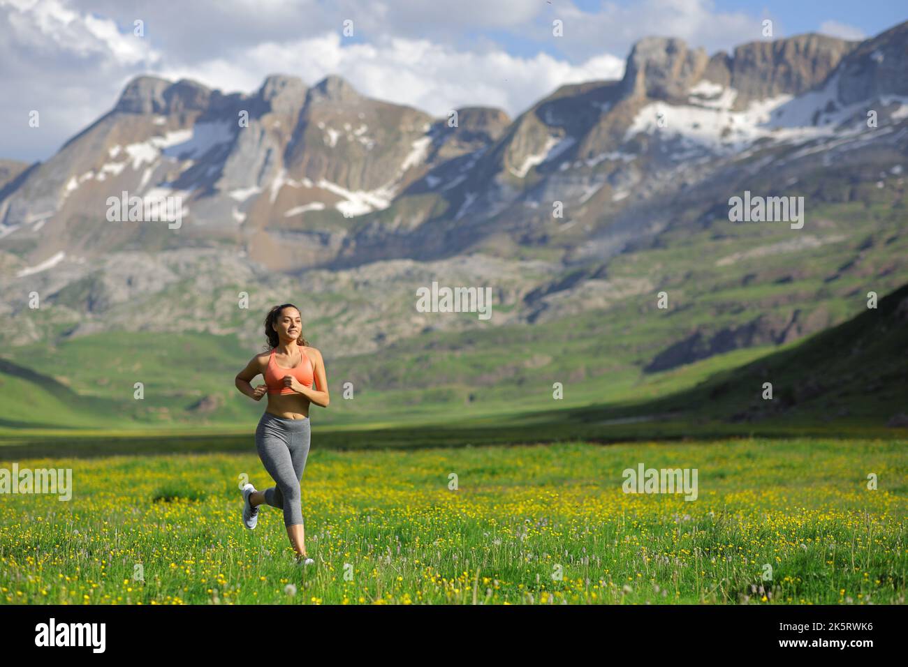 Full body portrait of a runner woman running in a green field in the ...