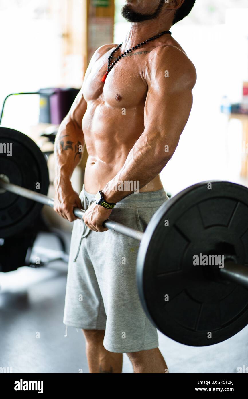 Vertical photo of an unrecognizable strong man lifting weights in a gym ...