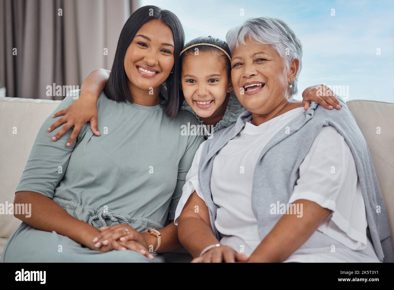 Happy and affectionate young mixed race family of three sitting on a sofa in the living room at ...