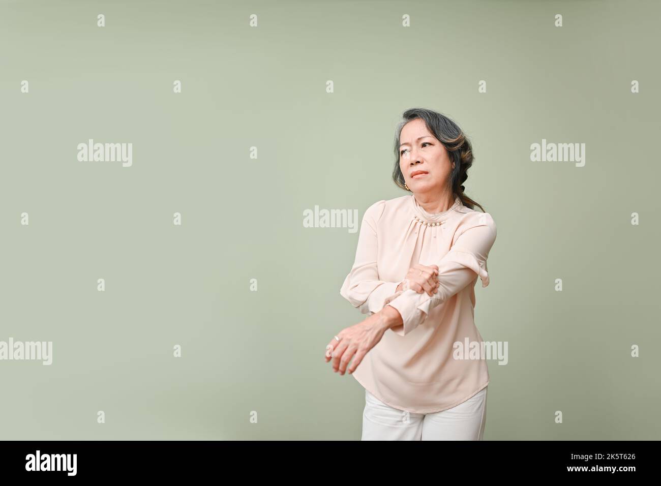 A distressed elderly Asian woman suffering from arm pain, massaging her ...