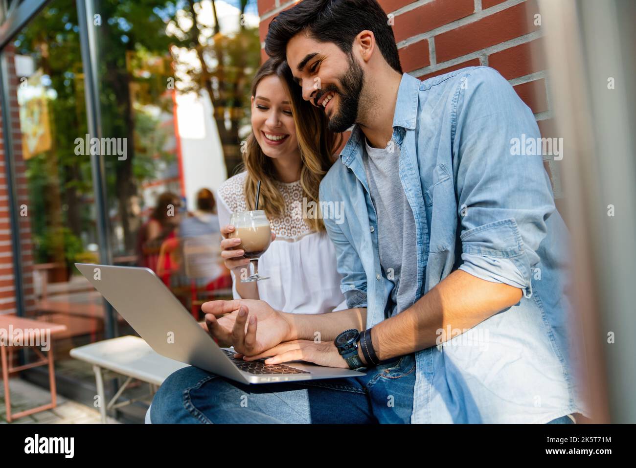 Couple sitting at cafe smiling, using laptop, spending time with ...
