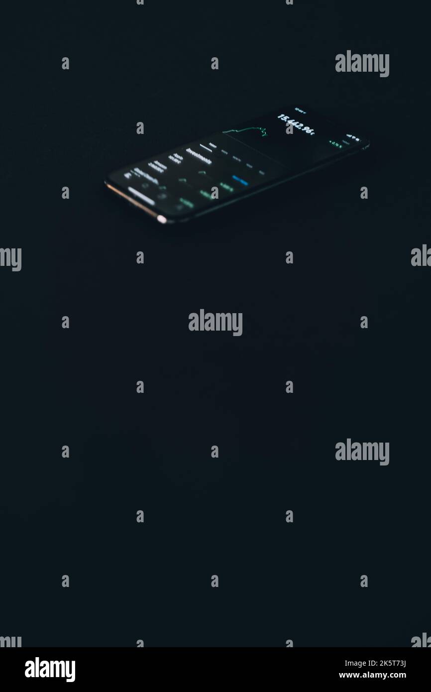 a vertical of a cell phone laying on a black surface displaying a trade ...