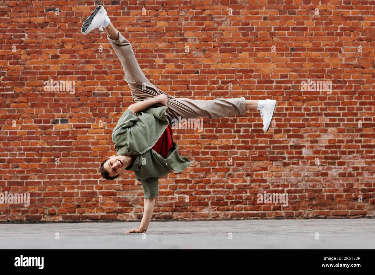 Full length shot of young man doing hip-hop handstand pose and smiling ...