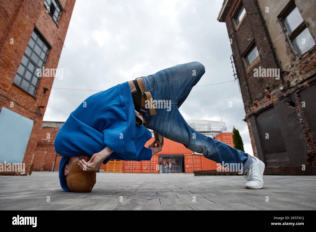 Full length shot of young man doing breakdance pose in urban factory ...