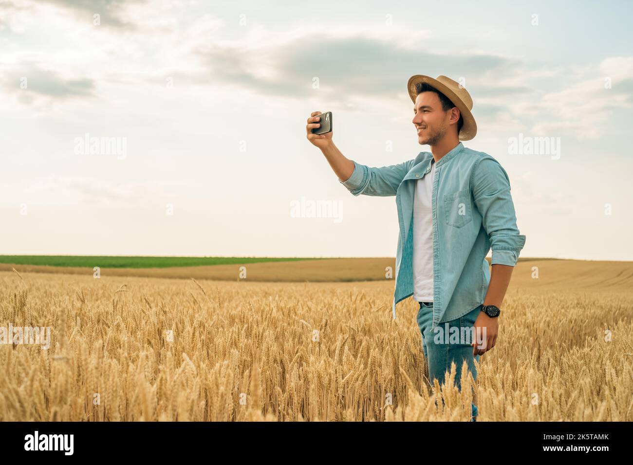 Happy farmer photographing crops with phone while standing in his ...