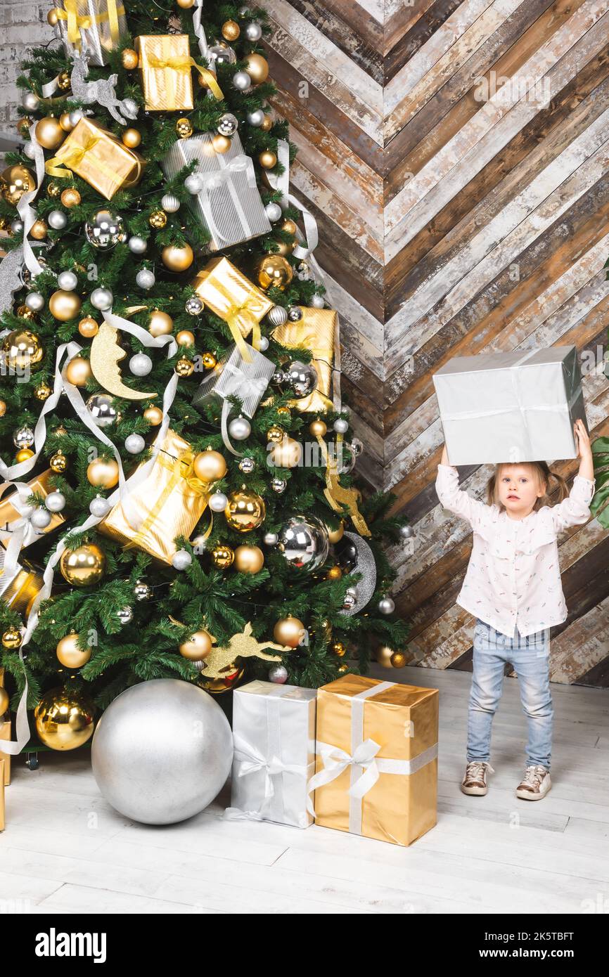 Portrait of elementary age girl standing beside christmas tree holding ...