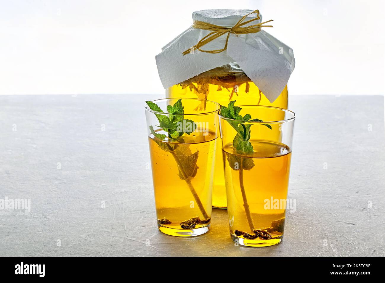 A jar of kombucha and two glass cups of kombucha are decorated with ...
