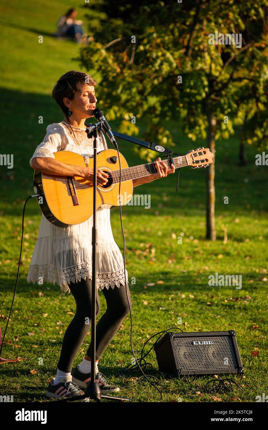 Lone female street musician with acoustic guitar performing in park in ...