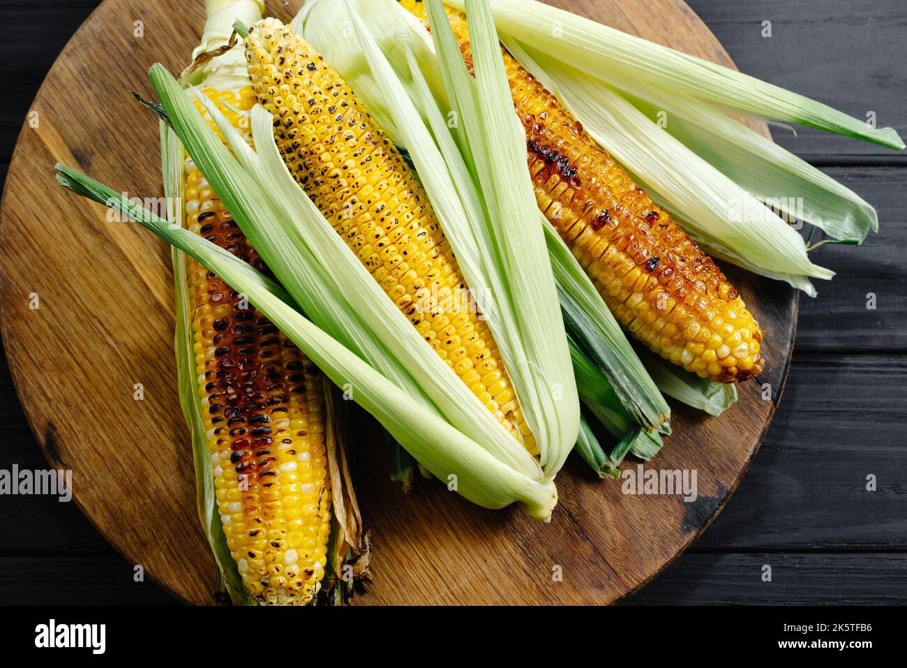 A cauldron of corn roasted over charcoal on a wooden board. Whole corn ...