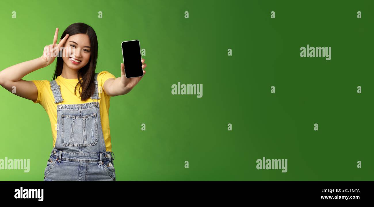 Cute carefree asian brunette showing application on smartphone screen ...