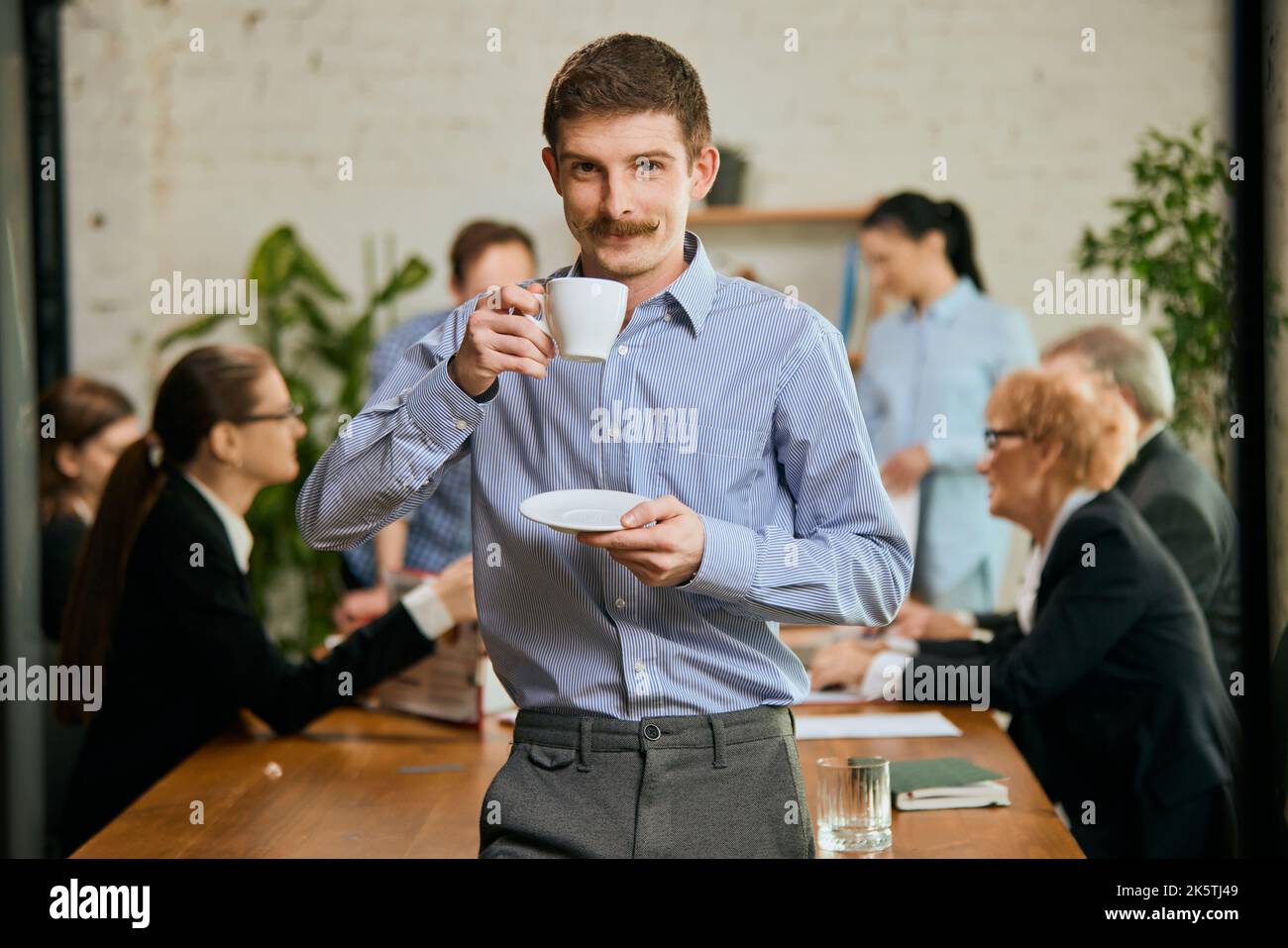 Happy young manager looking at camera and drinking coffee. Work in ...