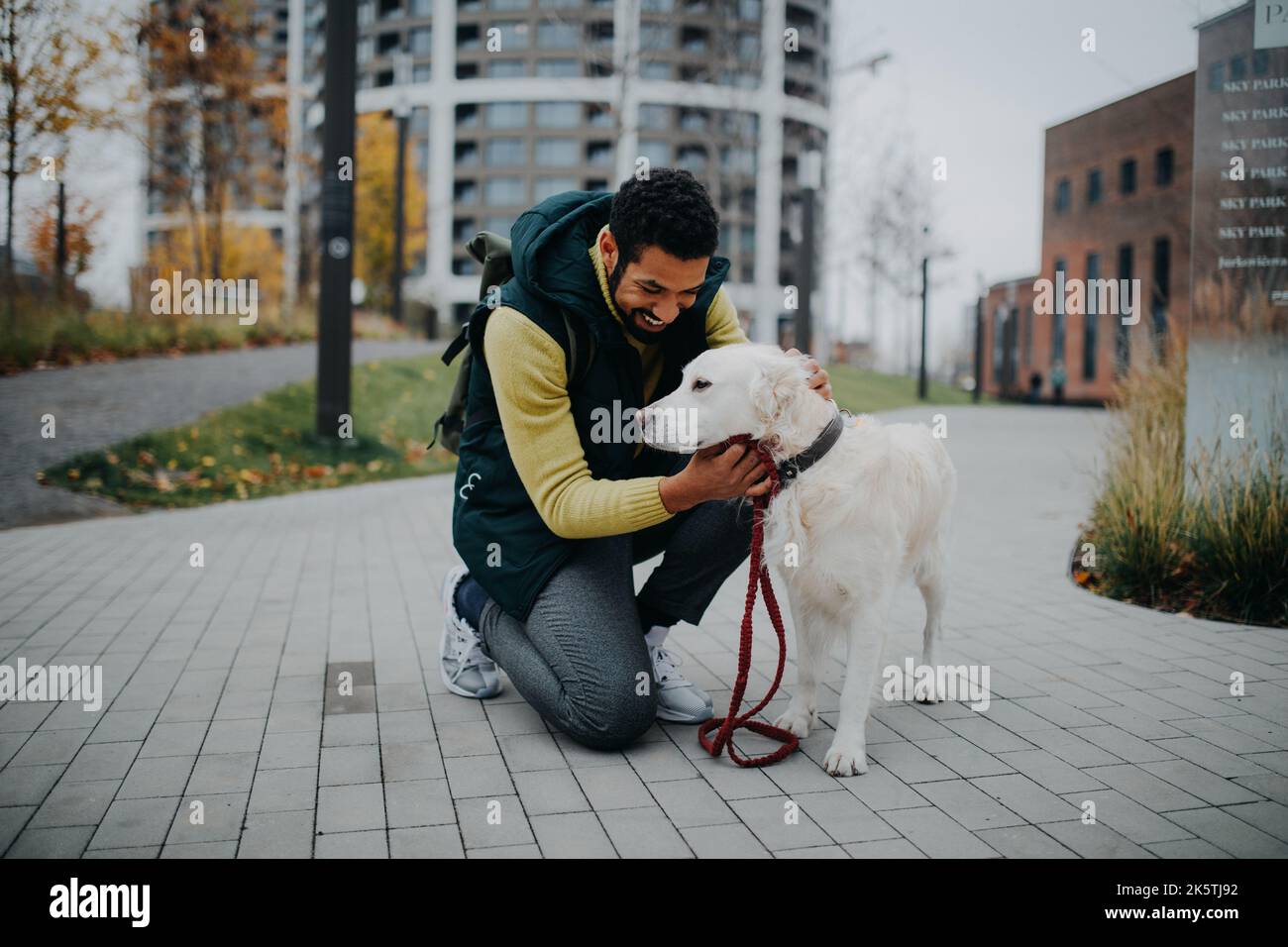 Happy young man stroking his dog outdoors in city park, during cold ...