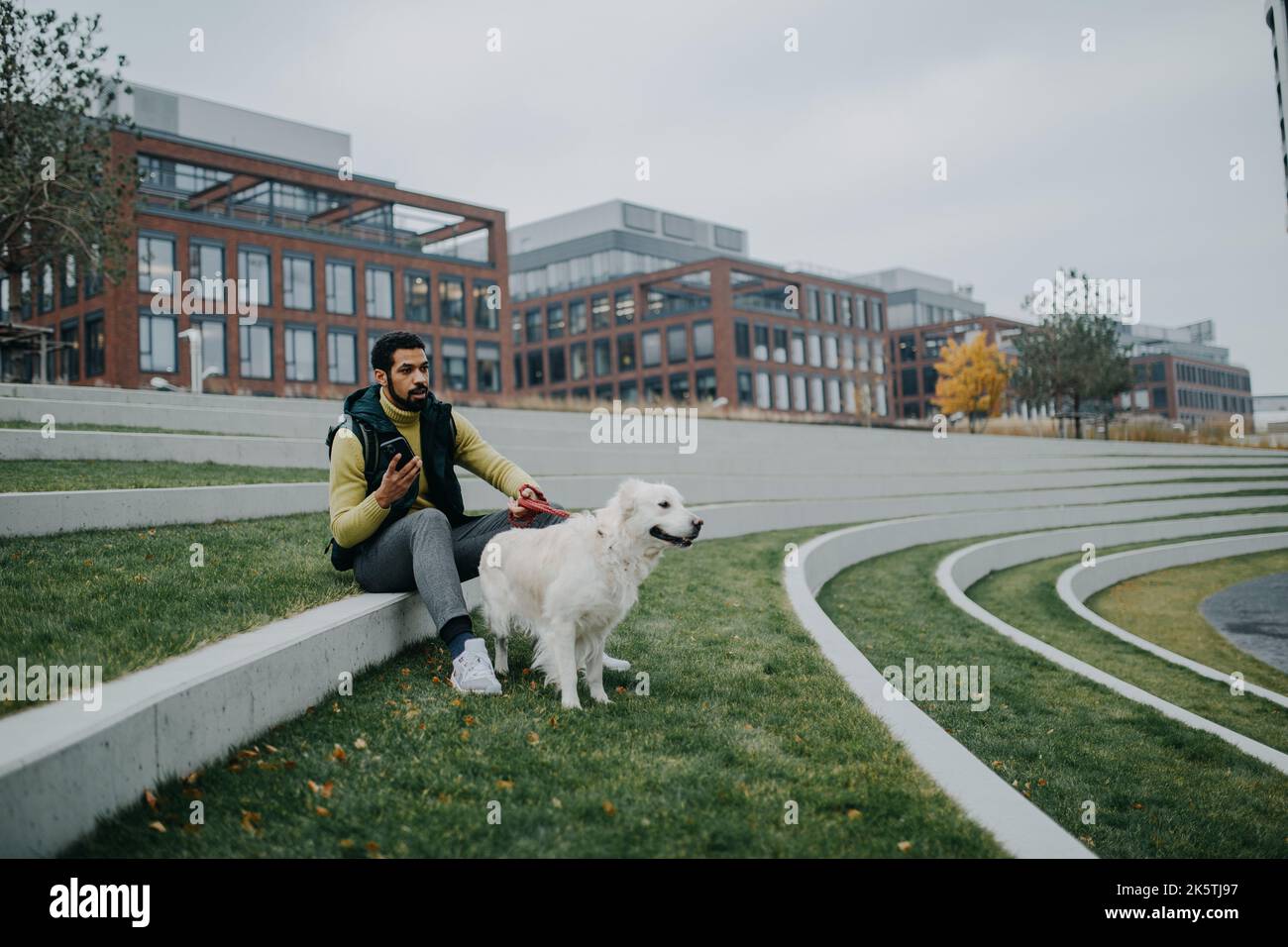 Happy young man resting and calling in urban city area during dog walk ...