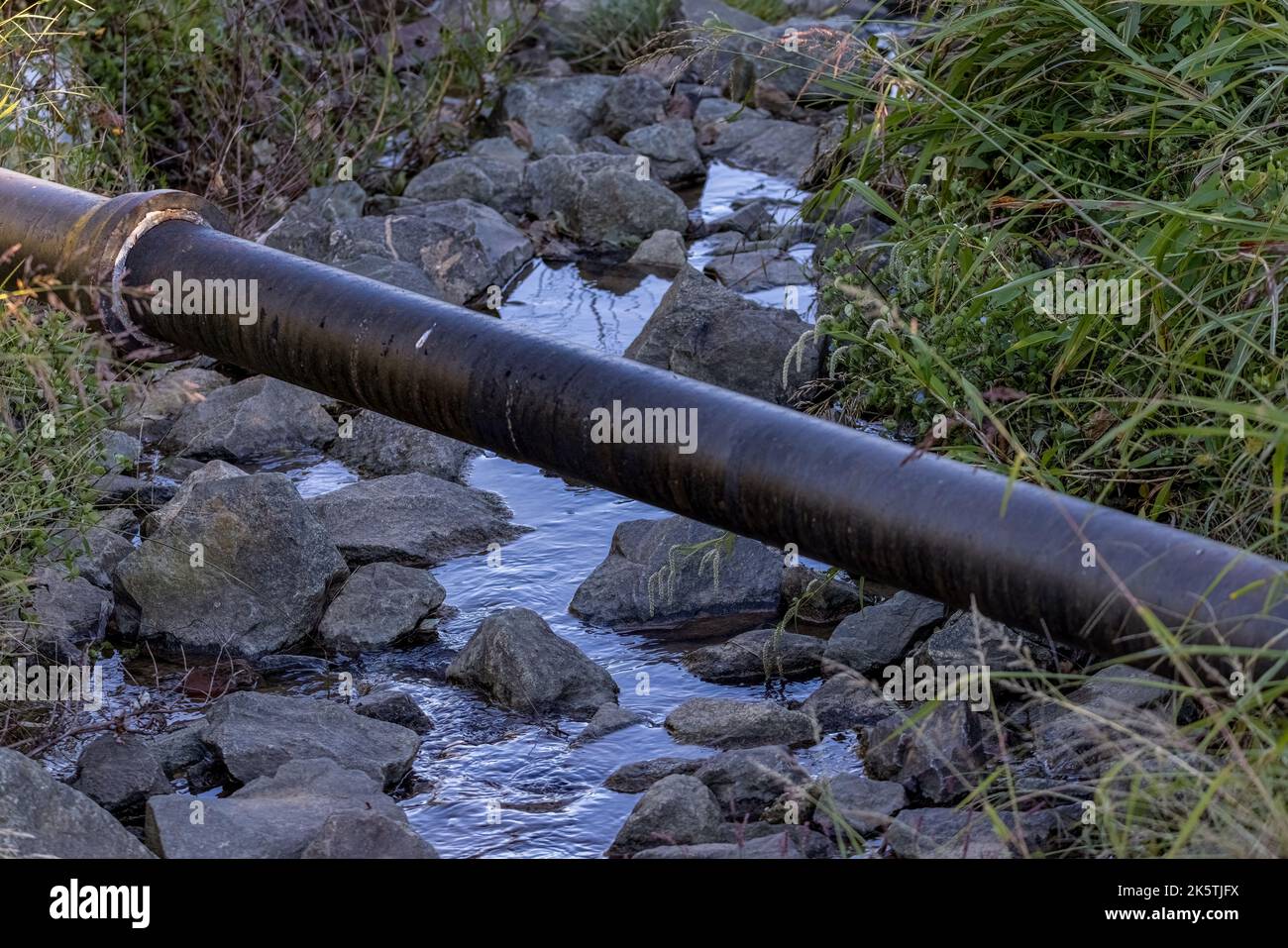 A black pipe crossing the rocky narrow stream Stock Photo - Alamy