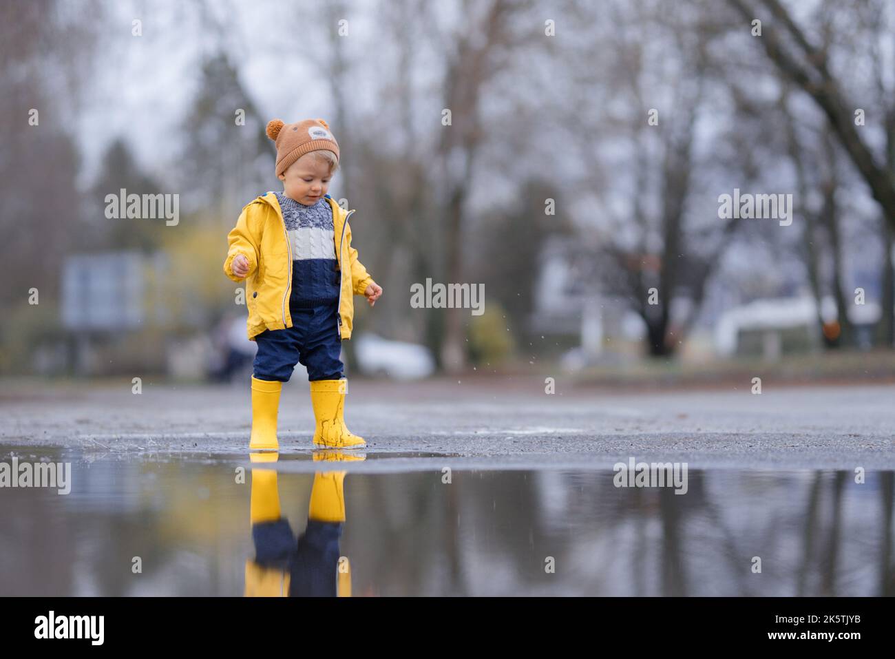 Happy little boy in yellow raincoat jumping in puddle after rain in ...
