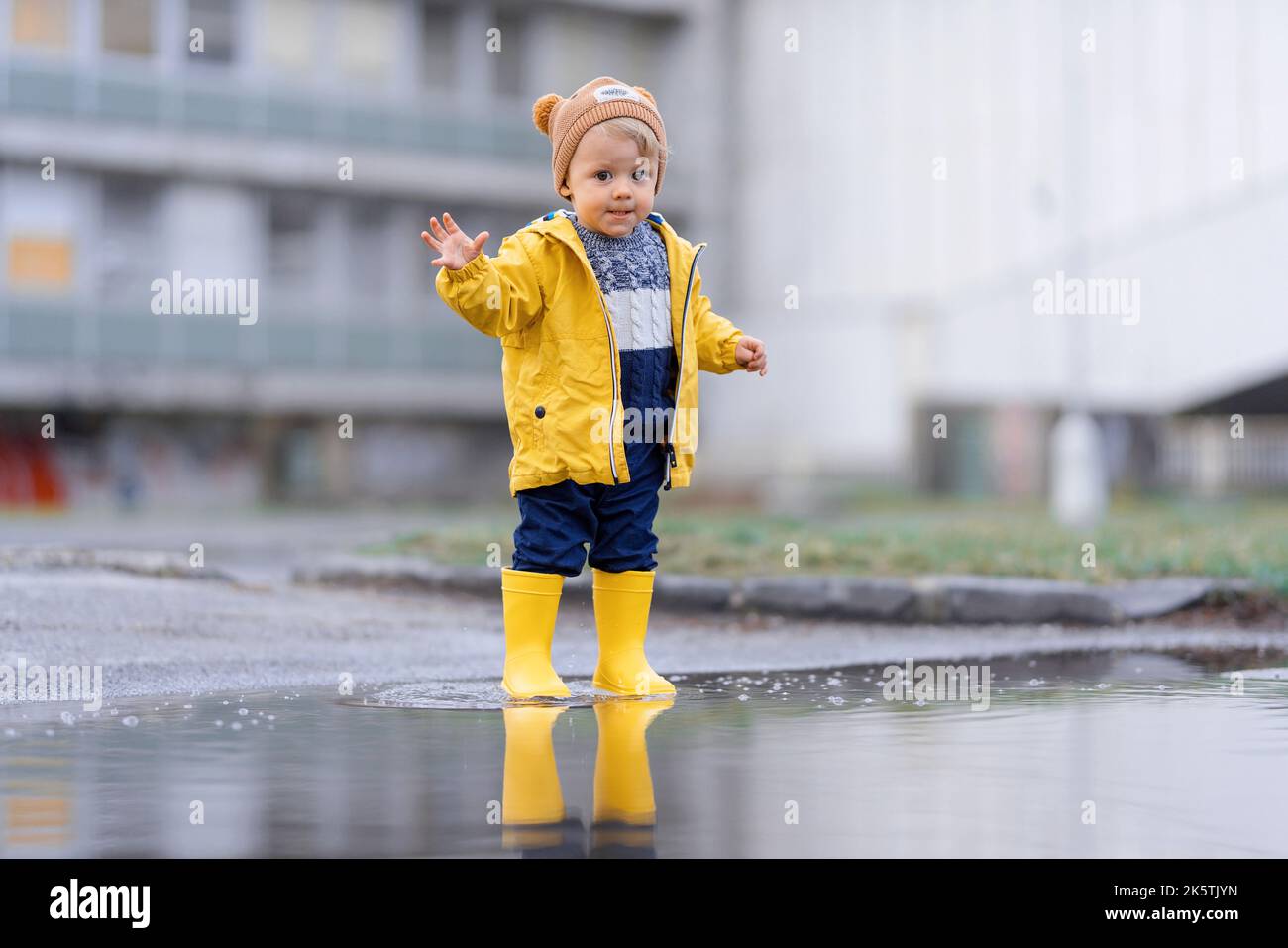 Happy little boy in yellow raincoat jumping in puddle after rain in ...