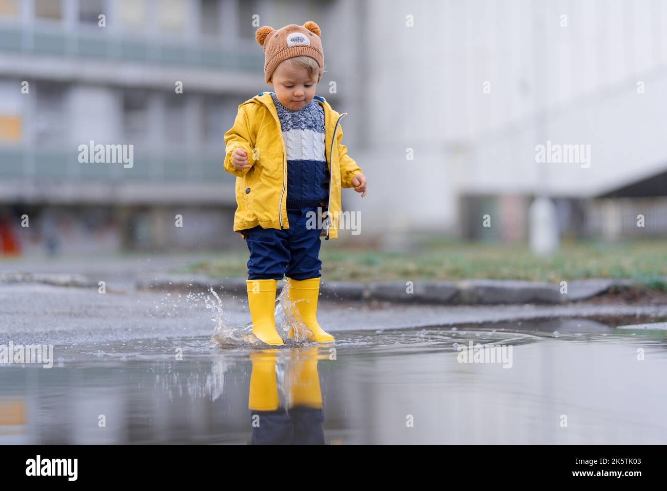 Happy little boy in yellow raincoat jumping in puddle after rain in ...