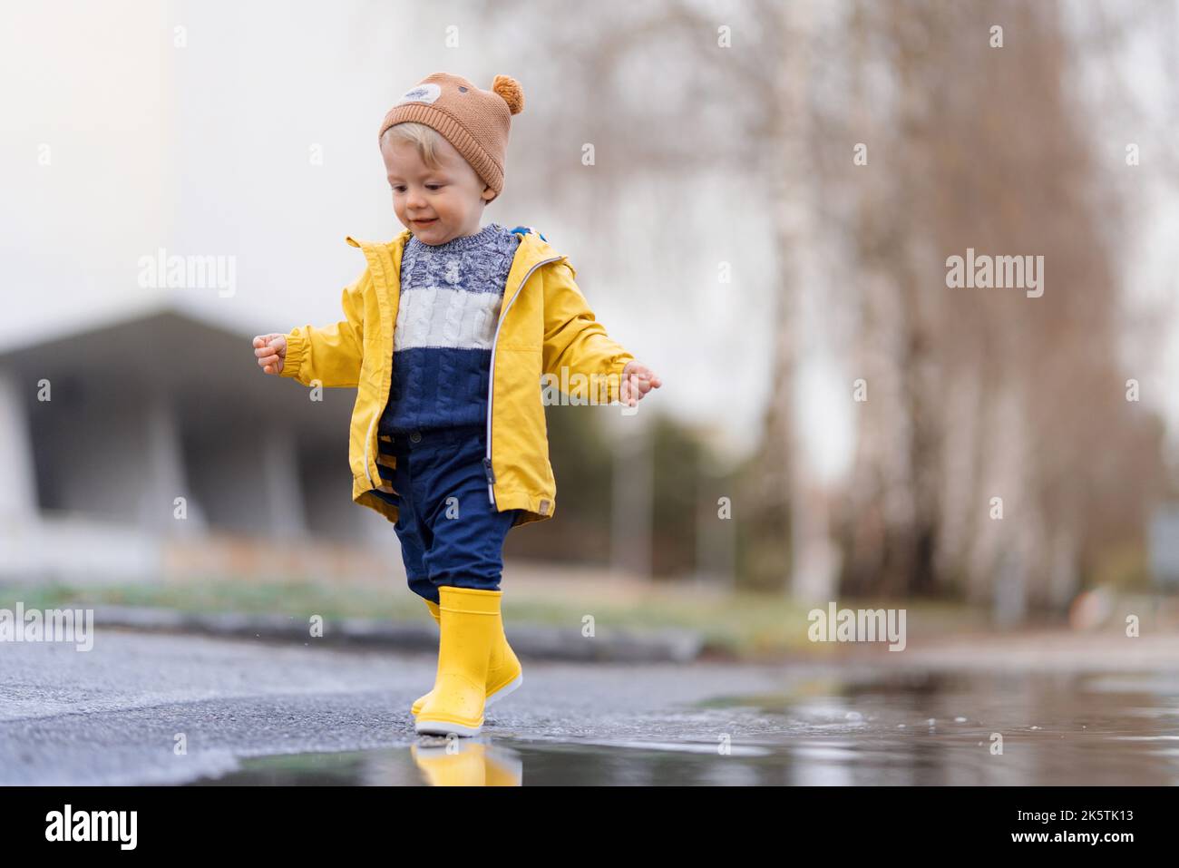 Happy little boy in yellow raincoat jumping in puddle after rain in ...