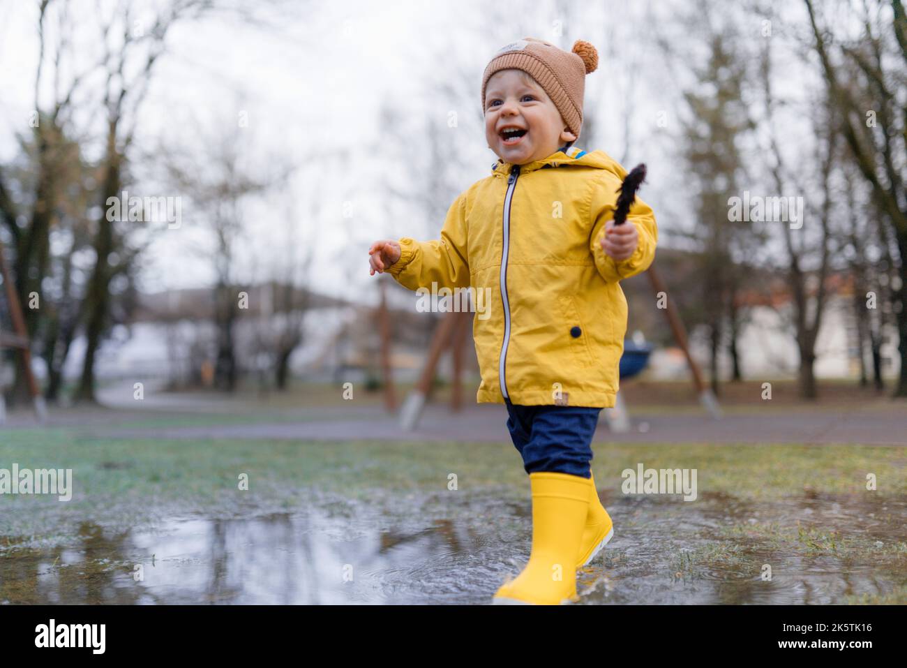 Happy little boy in yellow raincoat jumping in puddle and playing with ...